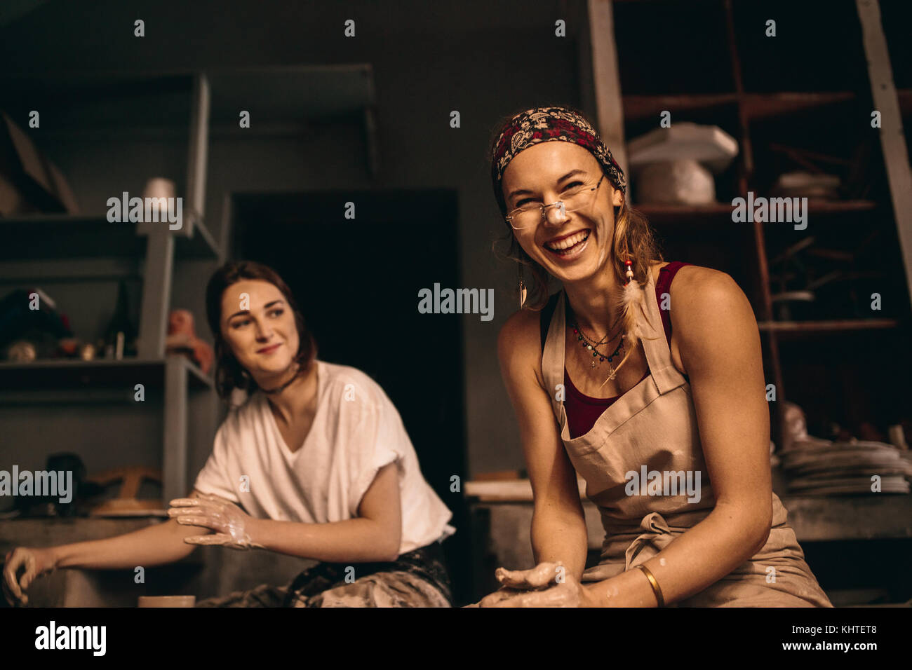 Two women making clay pots on potters wheel at workshop. Cheerful women ...