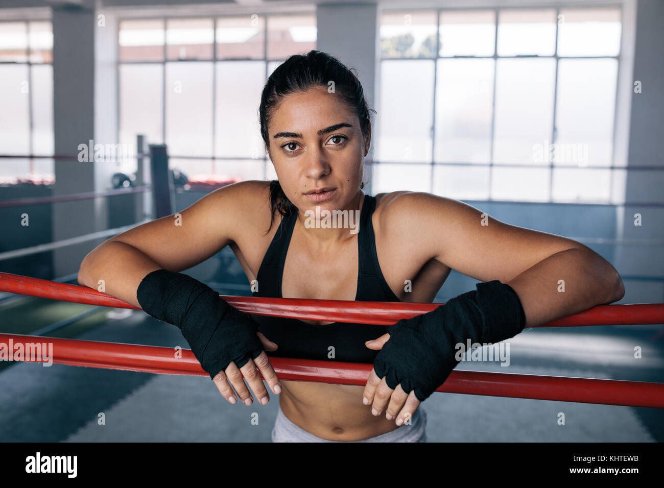 Female boxer standing inside a boxing ring. Boxer resting her arms on ...