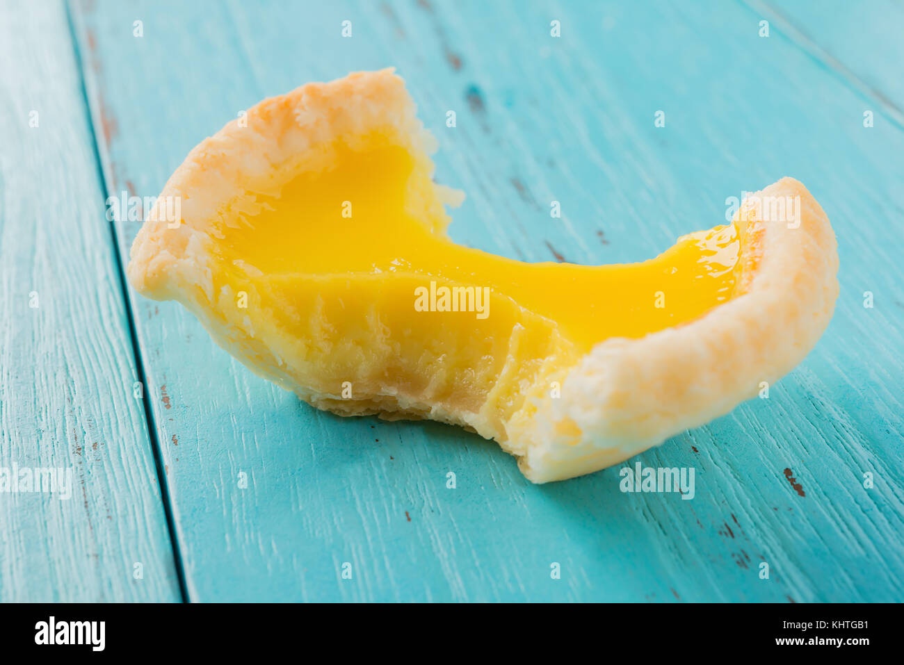 studio shoot of an egg tart with two big bites on a wood background ...