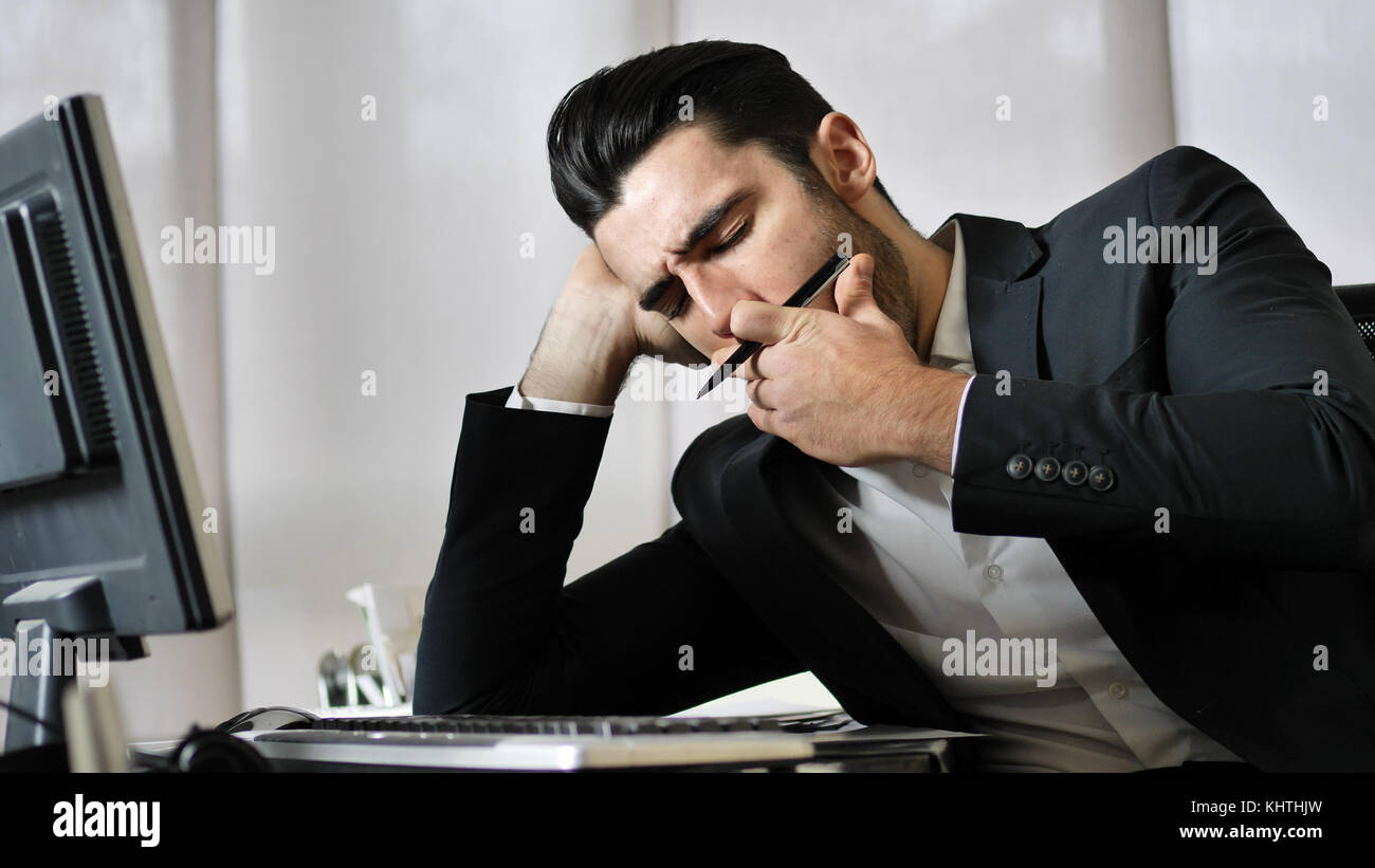 Tired bored young businessman sitting at his desk in front of his ...