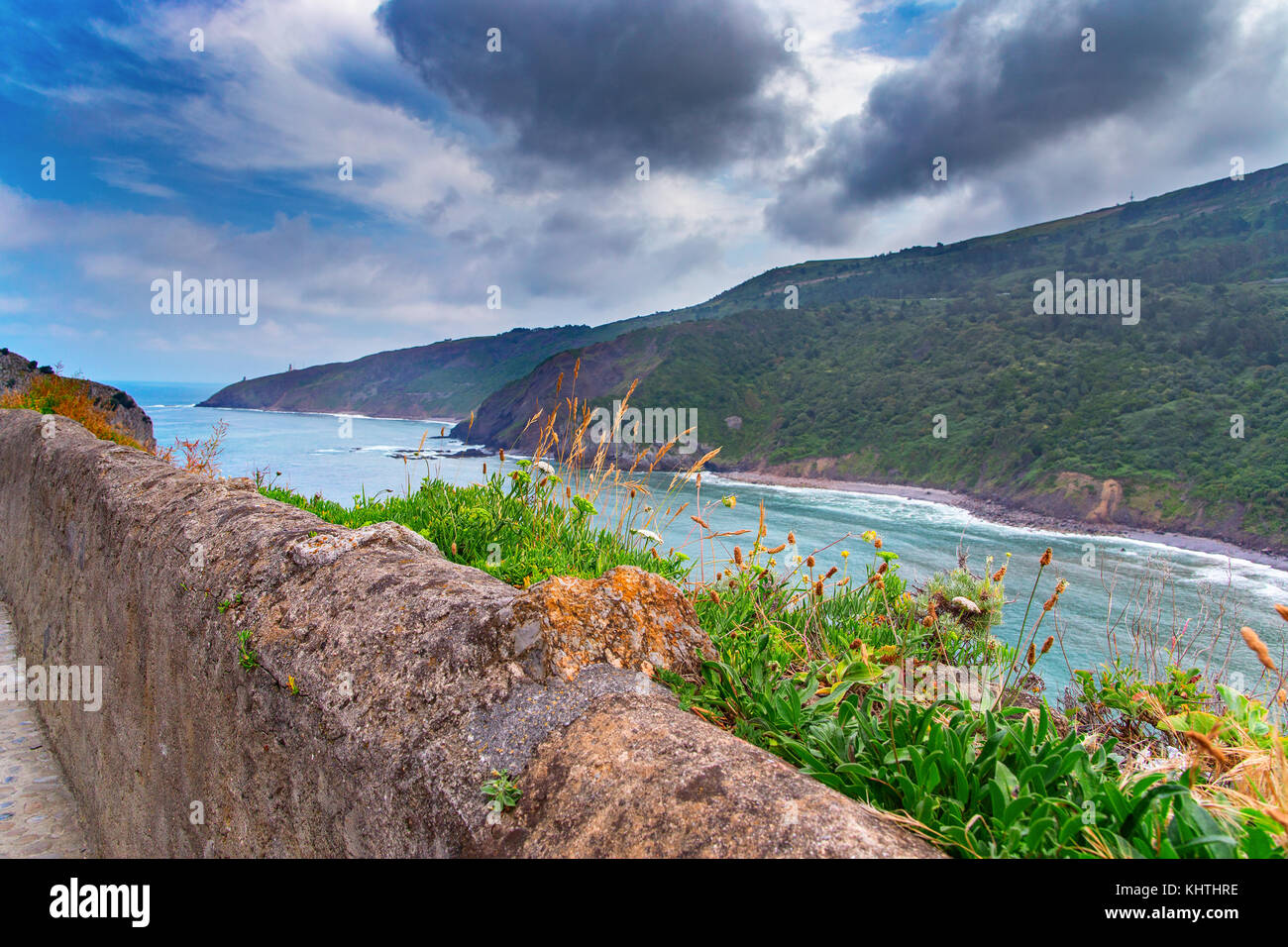 View of a sea bay from the high coast. A stone parapet and a green ...