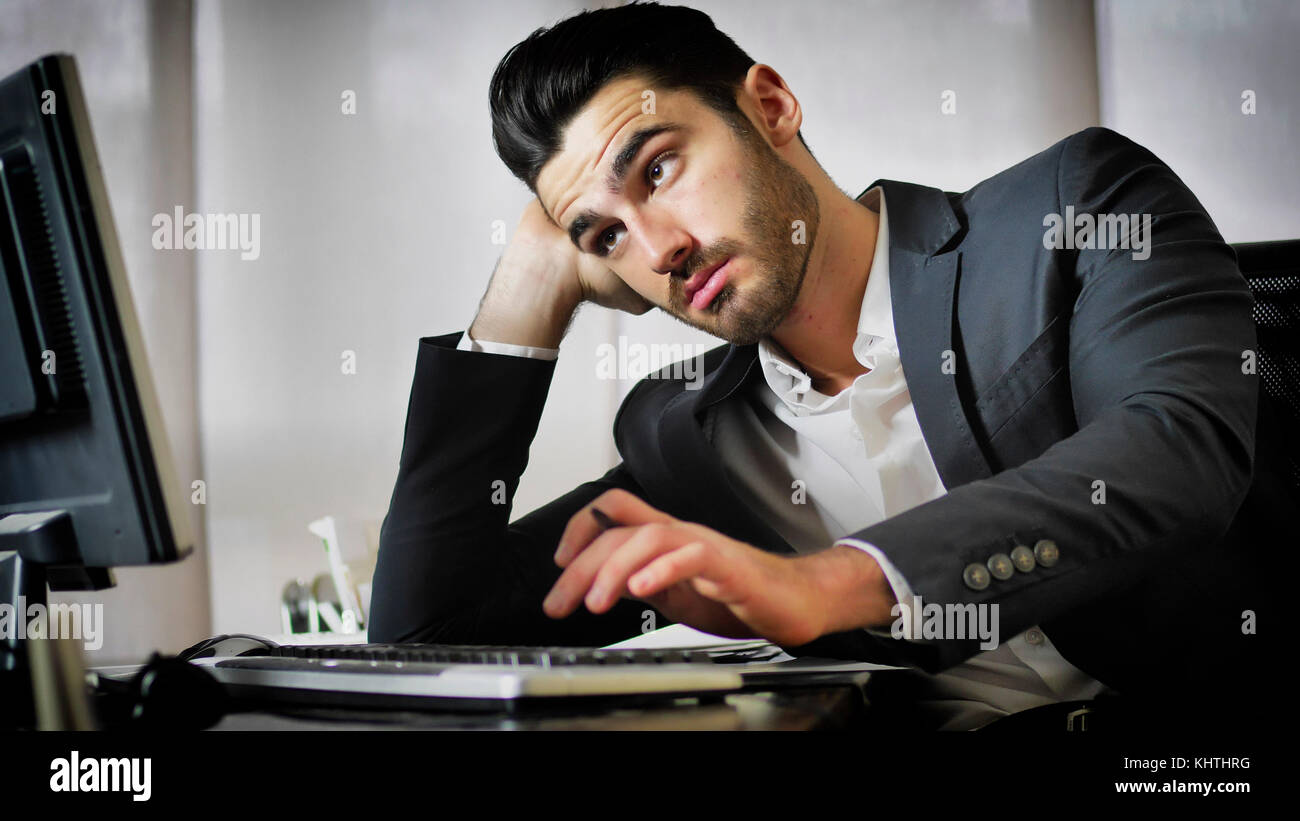 Tired bored young businessman sitting at his desk in front of his ...