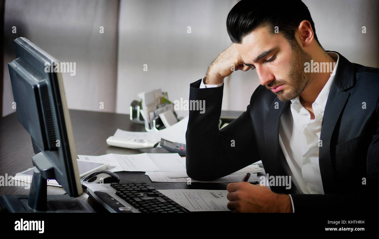 Tired bored young businessman sitting at his desk in front of his ...