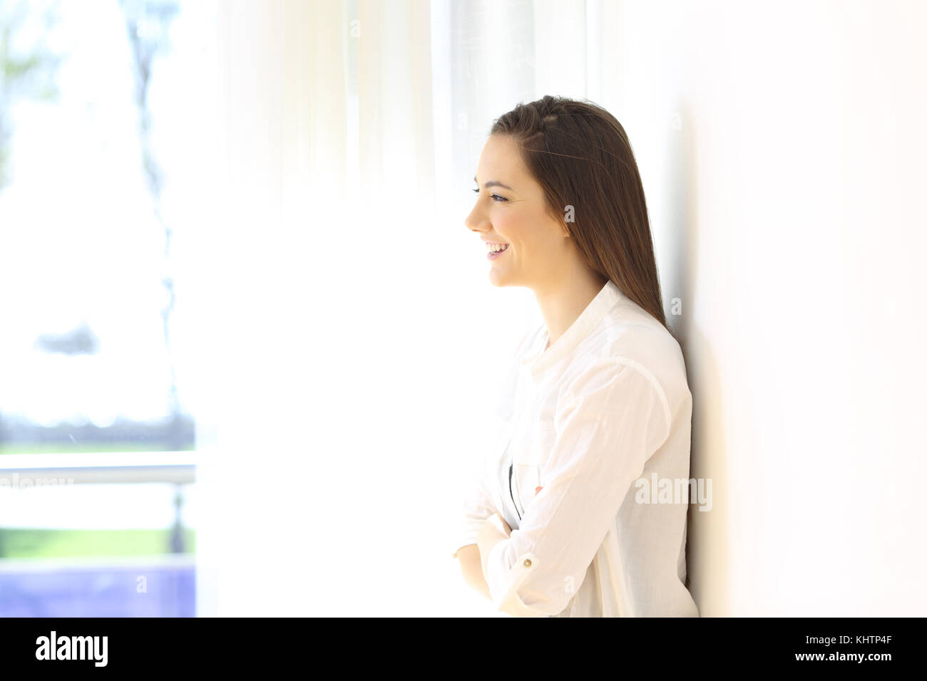 Side view portrait of a proud woman looking through a window at home ...