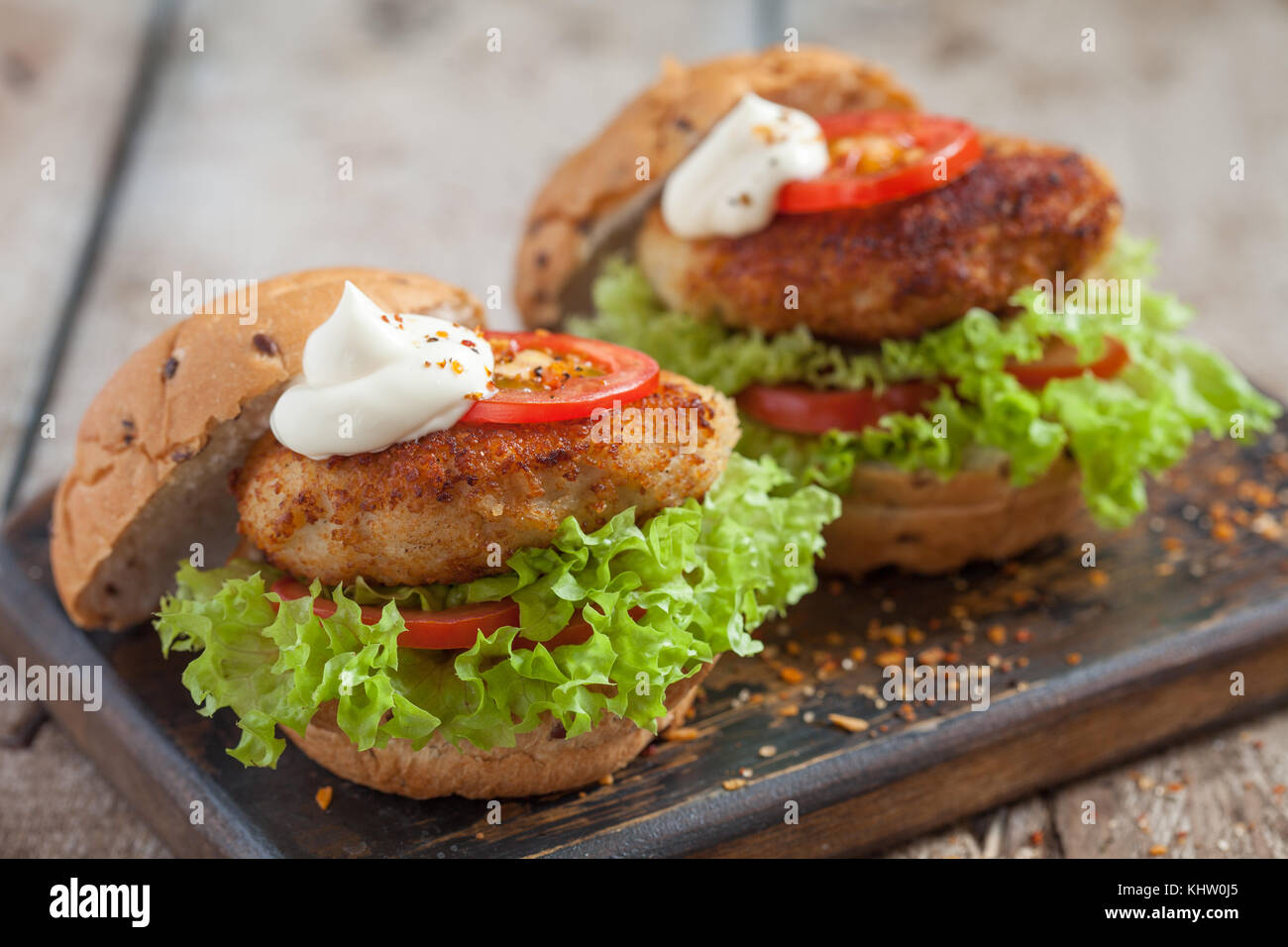 Two chicken burgers with vegetables on a wooden table Stock Photo - Alamy