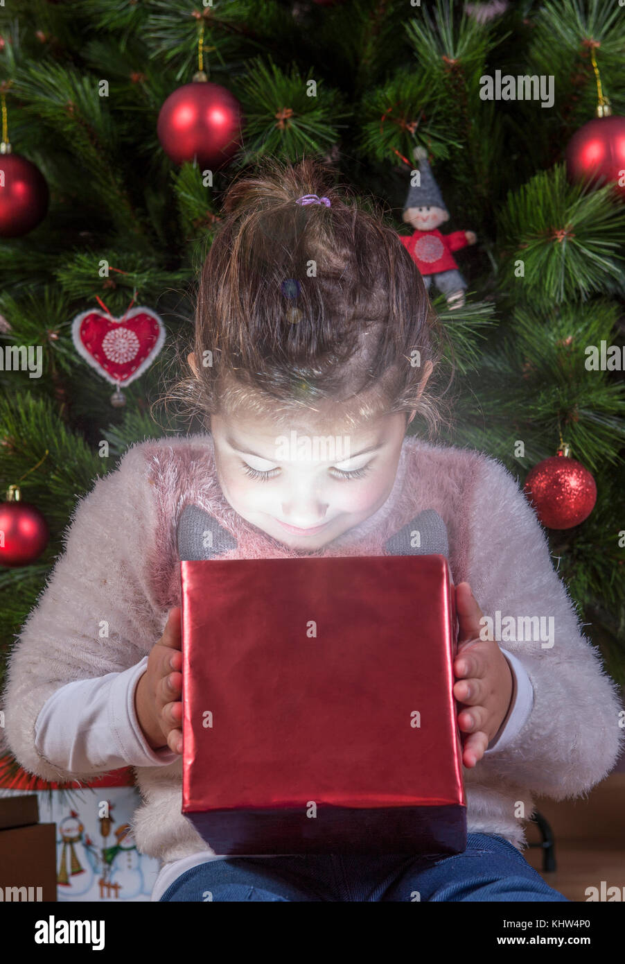 Little girl opening her present under Christmas tree. She is ...