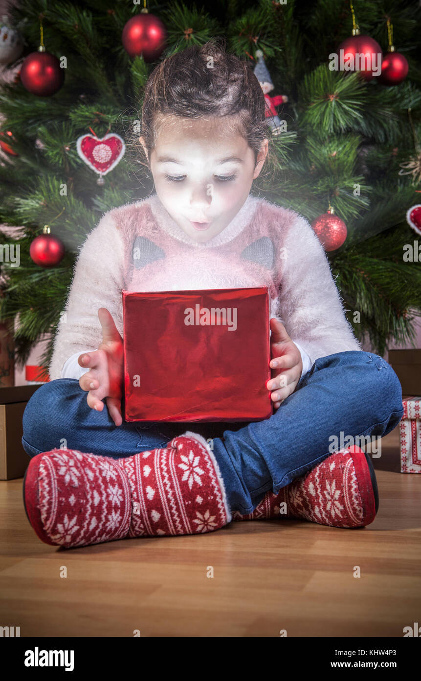 Little girl opening her present under Christmas tree. She is ...