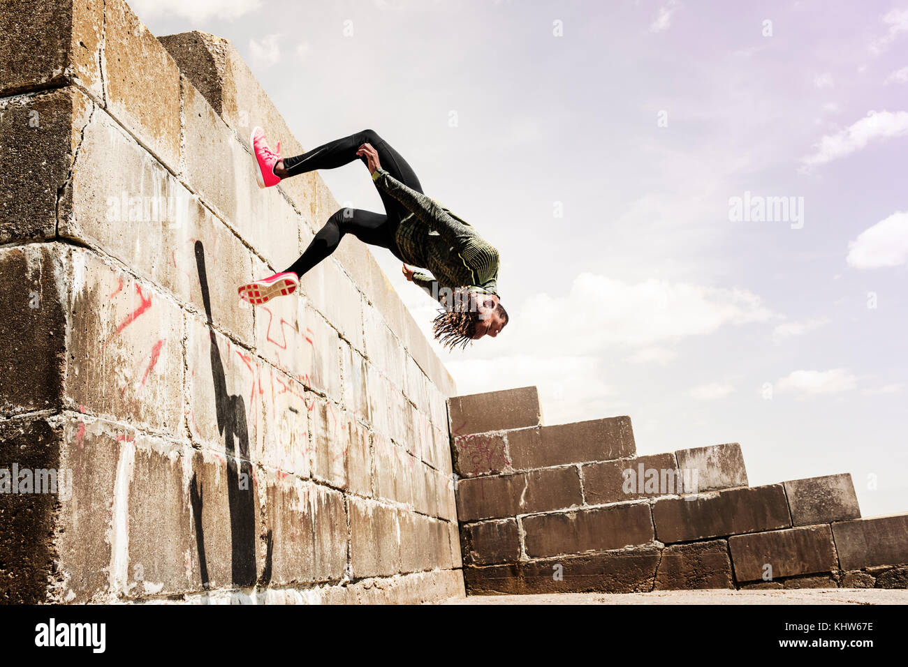 Young man, free running, outdoors, somersaulting from side of wall ...