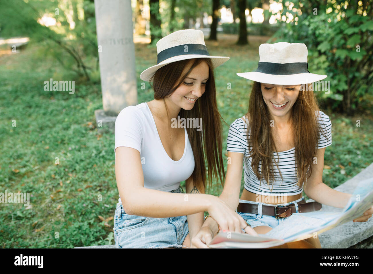 Two young female friends sitting on bench pointing at map in park Stock ...