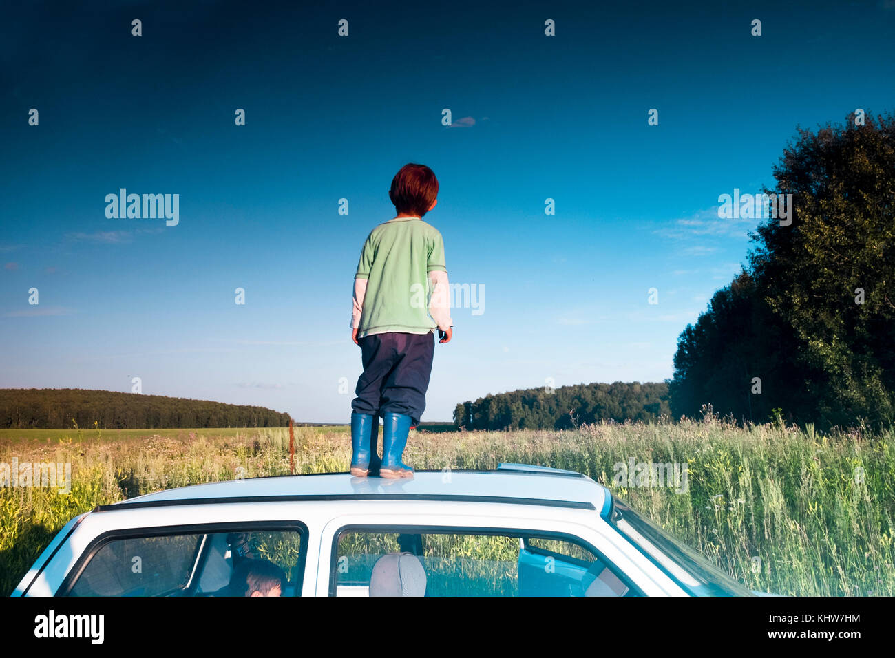 Young boy standing on car, looking at rural view, rear view, Ural ...