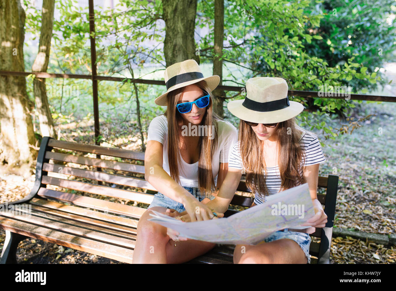 Two young female friends sitting on bench looking at map in park Stock ...