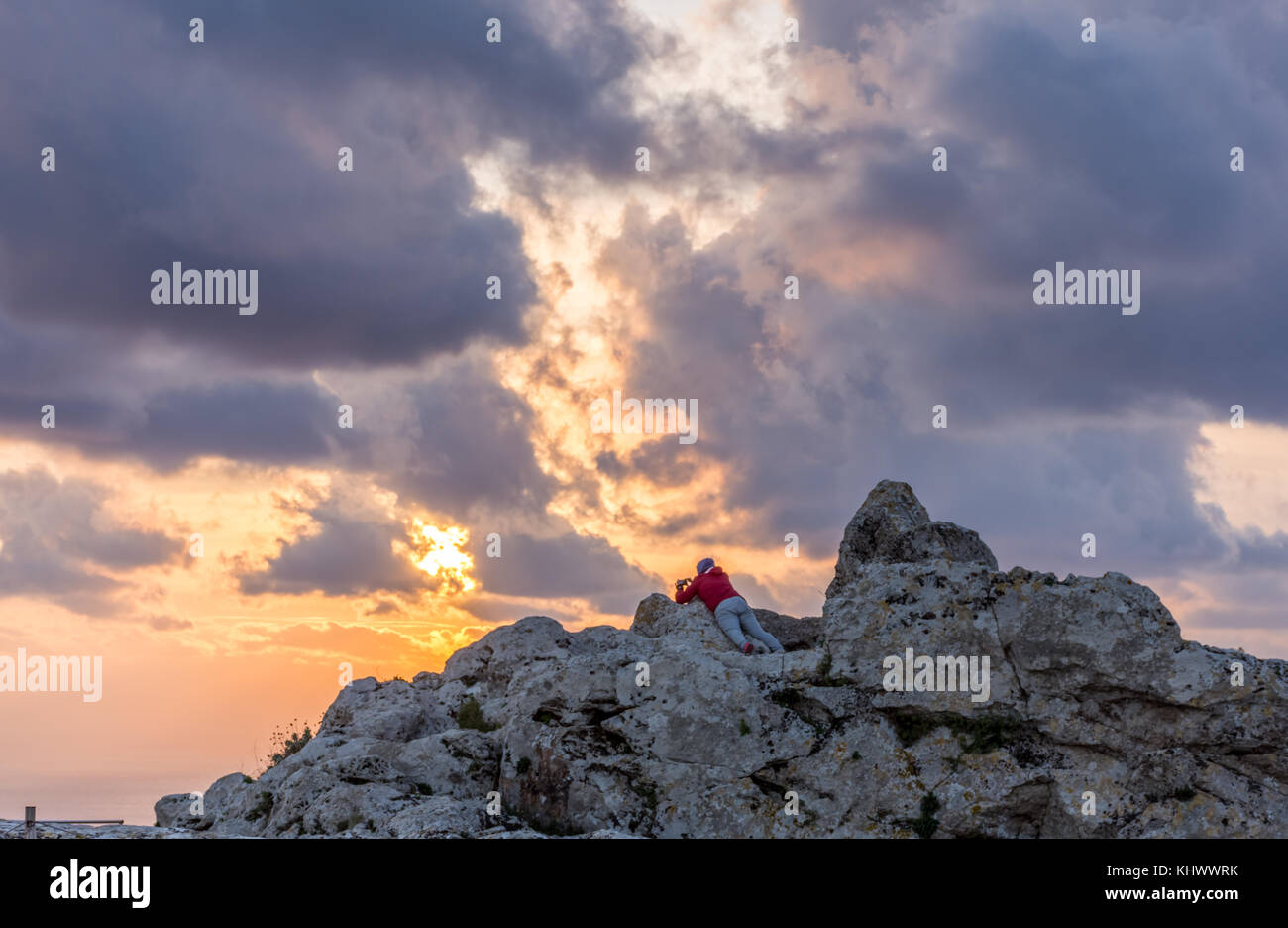 A woman resting on rocks at the edge of a 300 ft cliff photographing ...
