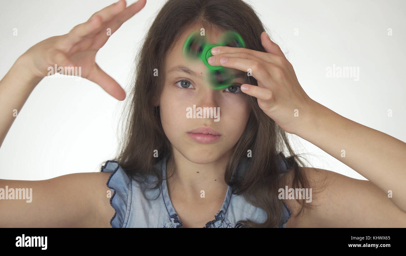 Beautiful cheerful teen girl playing with green fidget spinner on white ...
