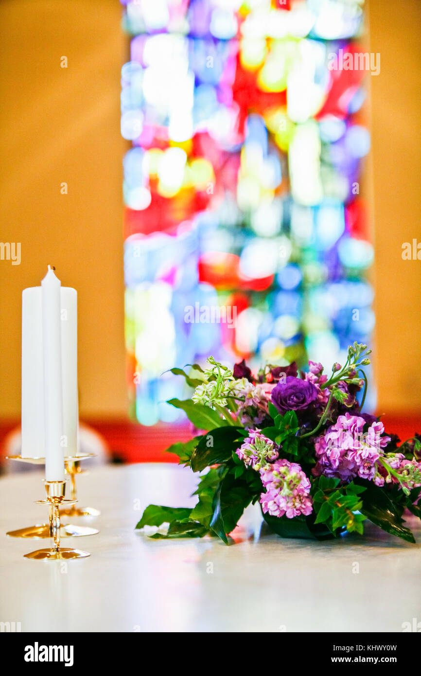 Candles and bouquet on table with burry colorful stained glass window ...