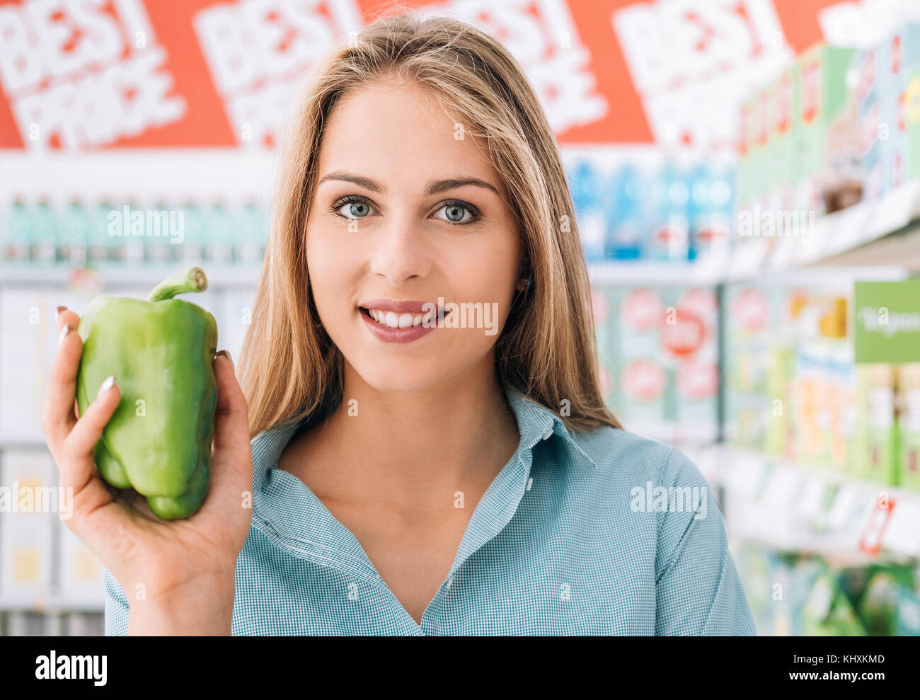 Smiling young woman shopping at the supermarket, she is holding a fresh ...