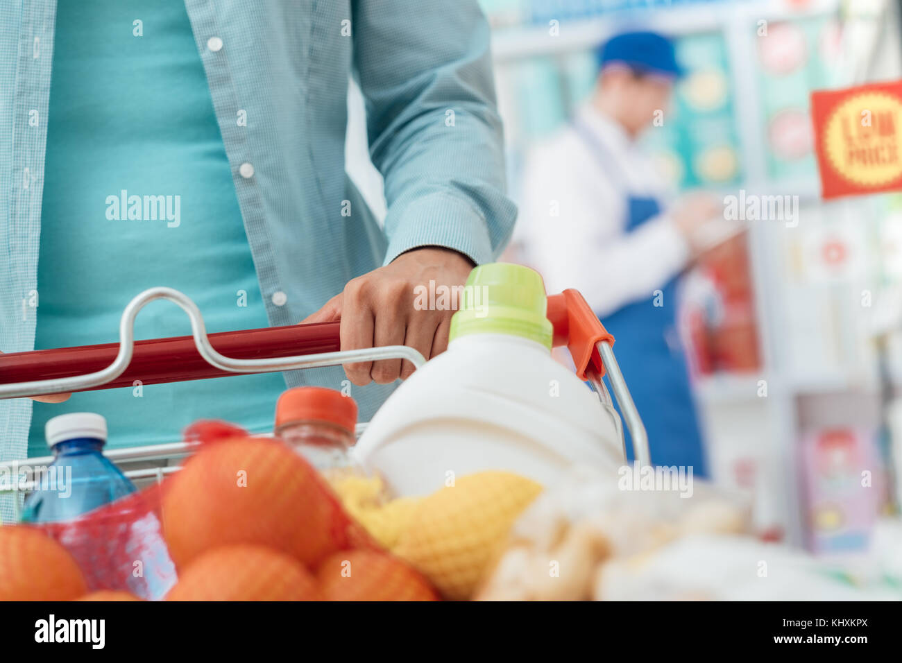 Woman shopping at the supermarket and pushing a full cart, clerk ...