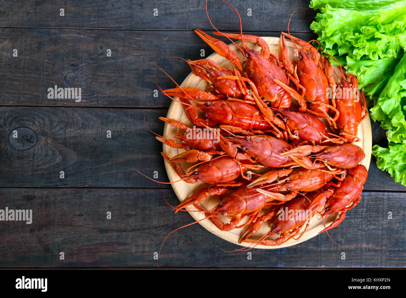 A pile of tasty boiled crawfish on a round wooden tray on a dark table ...