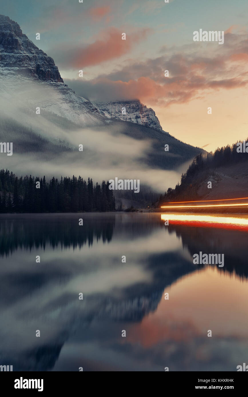 Mountain lake and traffic light trail with reflection and fog at sunset ...
