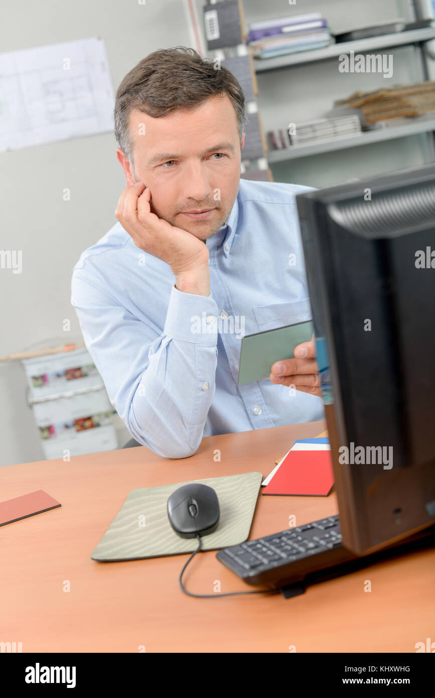 Man looking at computer, cross referencing Stock Photo - Alamy