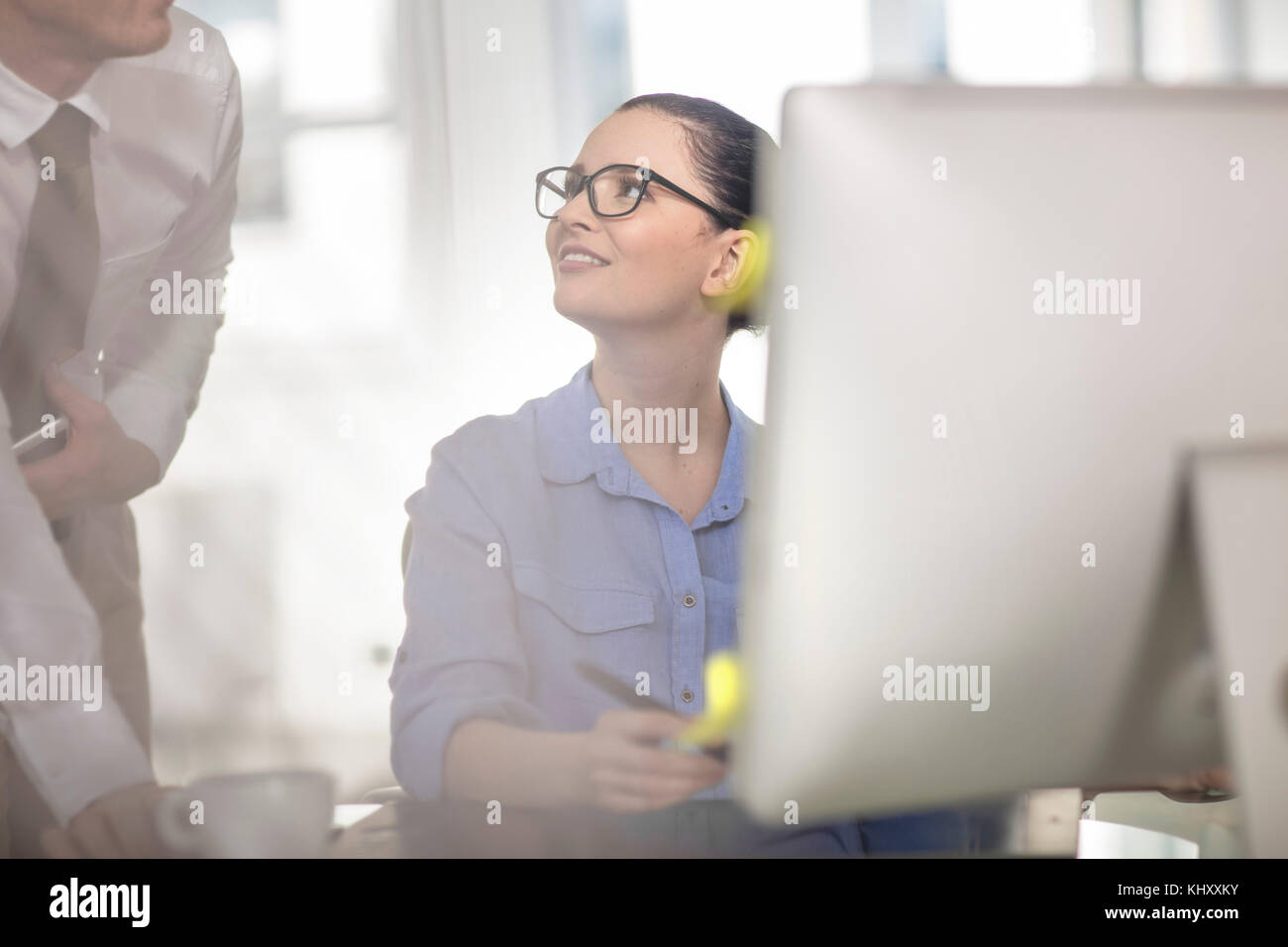 Young female office worker having discussion with colleague at desk ...