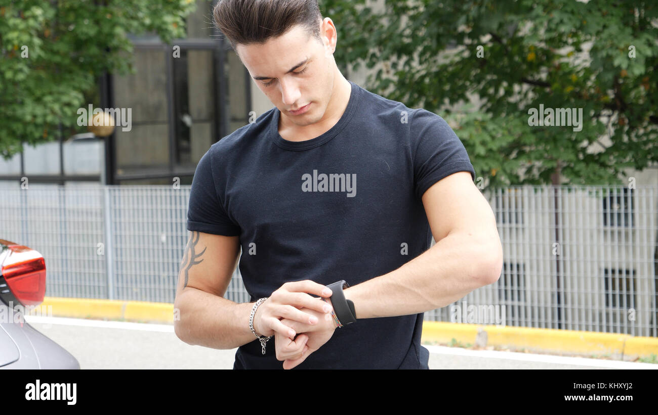 Casual muscular man watching smartwatch while standing on street Stock ...