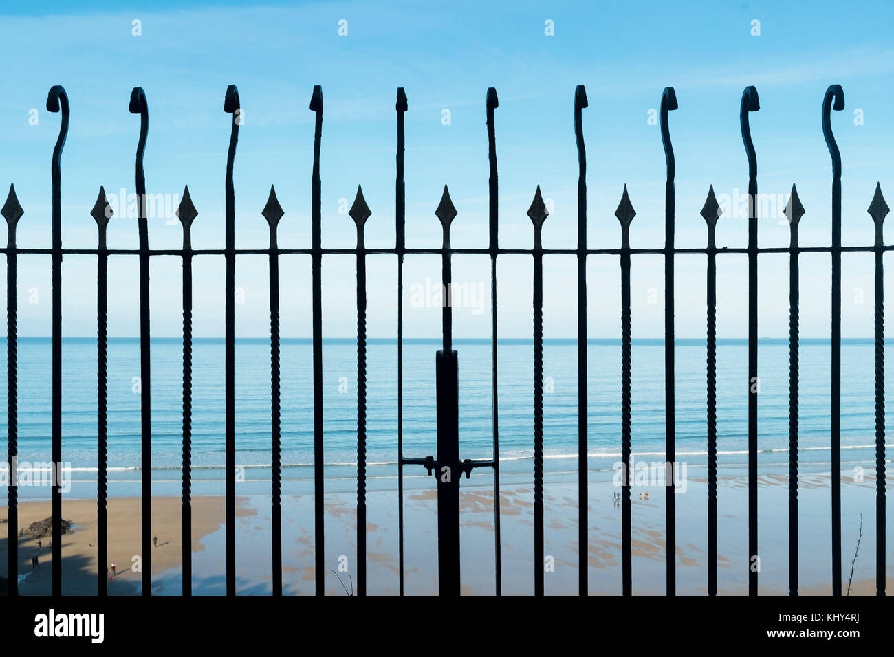An ornate metal railing seen in silhouette with a beach and the sea in ...