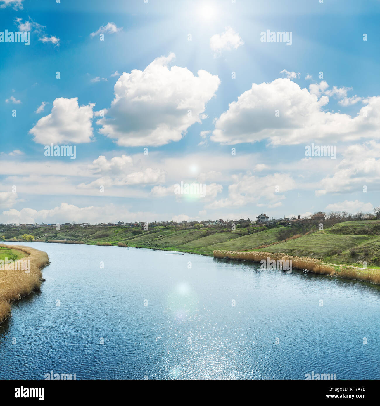 sun in blue sky over clouds and river with reflections Stock Photo - Alamy