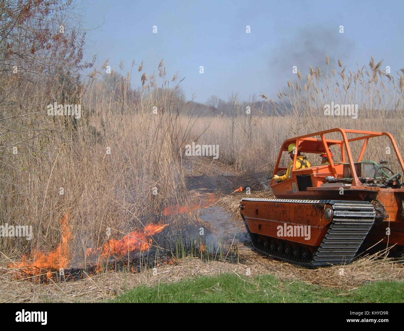 Fireman started a fire in the tall grass while driving in heavy tracked ...