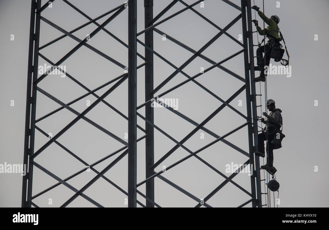 Two technicians work on a high voltage line high above the ground near ...
