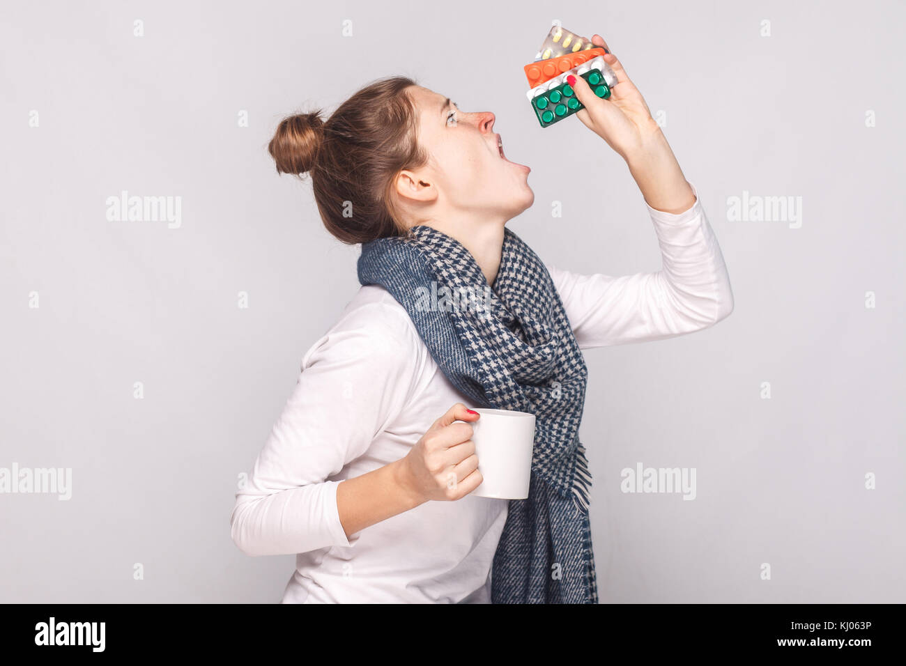 Sick young woman holding cup with tea, many pills and antibiotics ...