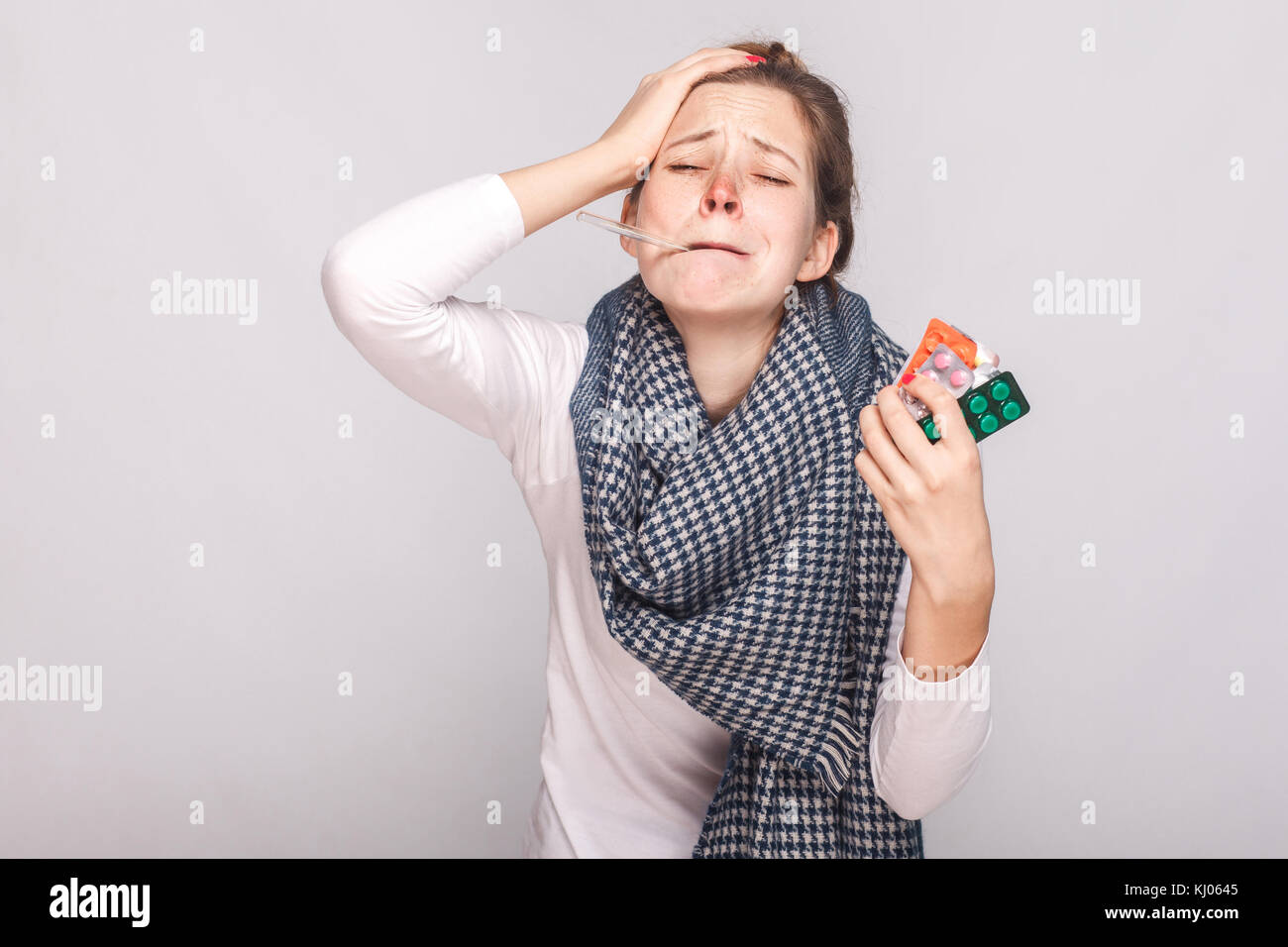 Young adult sick woman have temperature, holding many pills. Studio ...