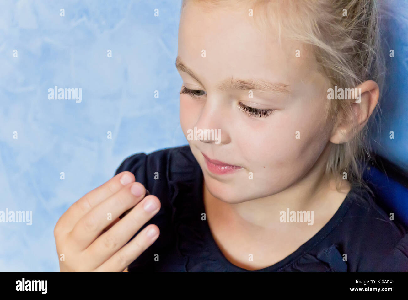 Cute eating girl with blond hair on blue background Stock Photo - Alamy