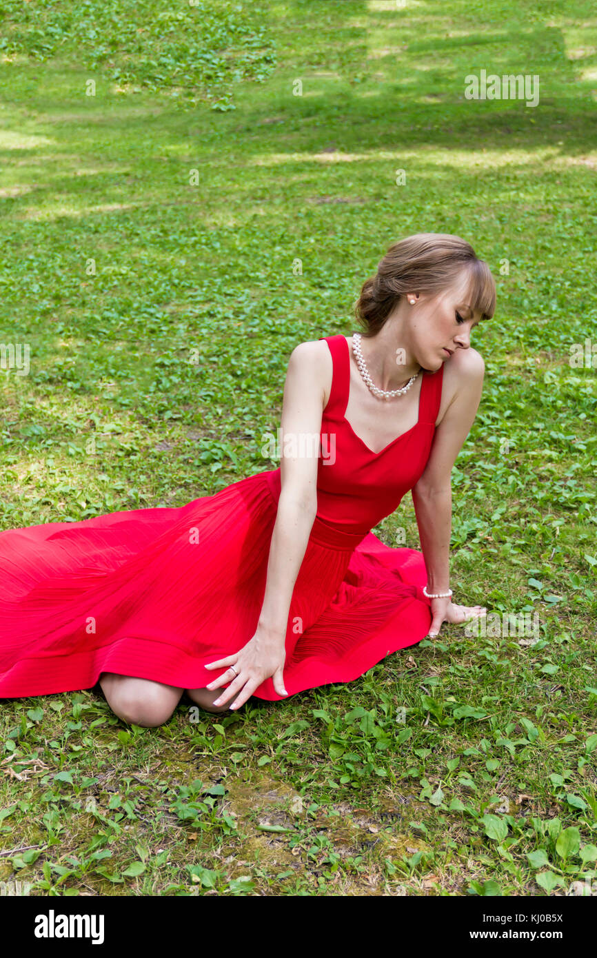 Beautiful lady in red are sittiing on green grass Stock Photo - Alamy