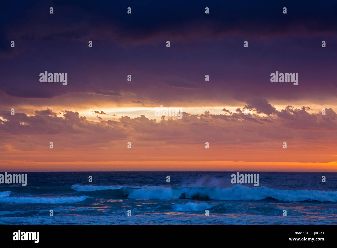 Distant clouds backdrop waves crashing on the beach Stock Photo - Alamy