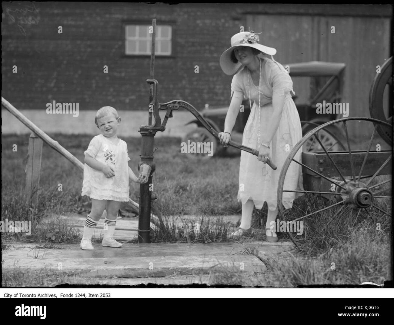 This photograph shows a woman operating a traditional water pump at a ...