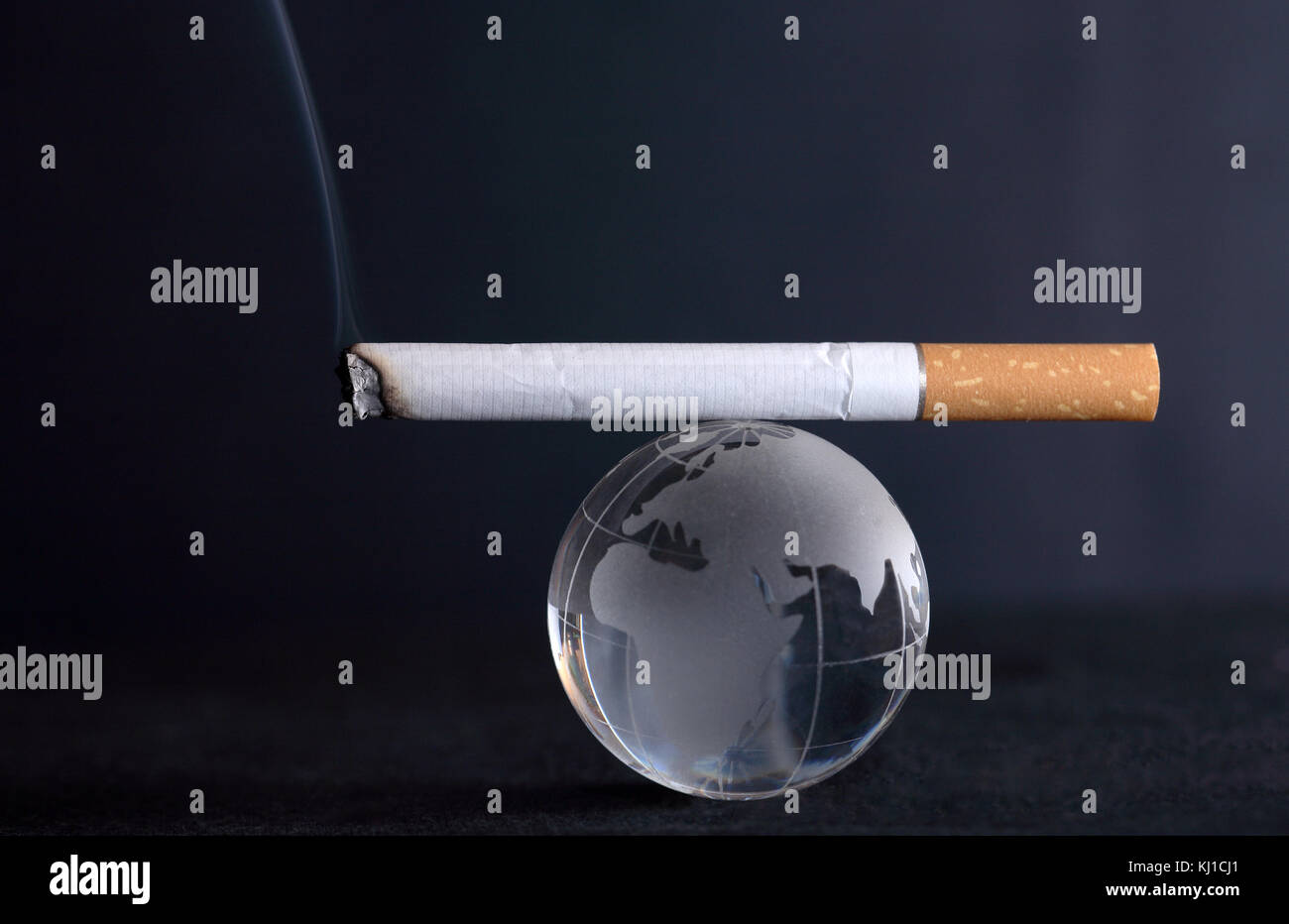 Conceptual balance: smoking cigarette lying on glass globe on dark ...