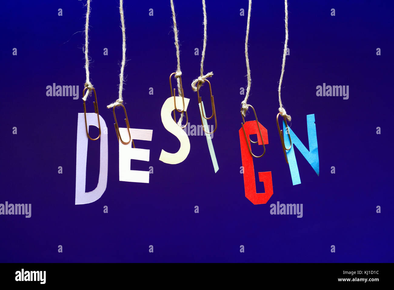 Word DESIGN made from color paper letters hanging with ropes on blue ...