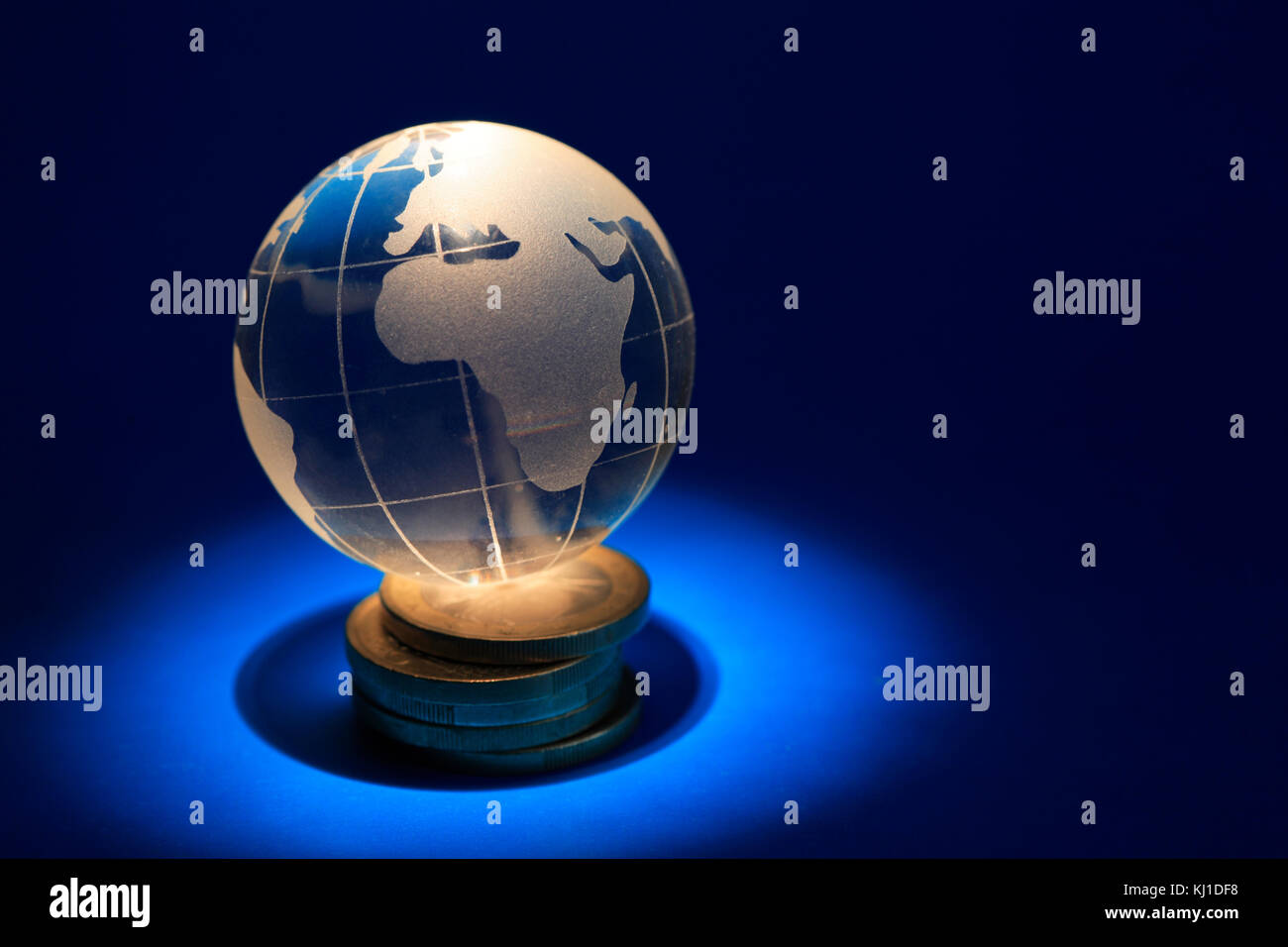 Glass globe lying on stack of coins on dark blue background with ...