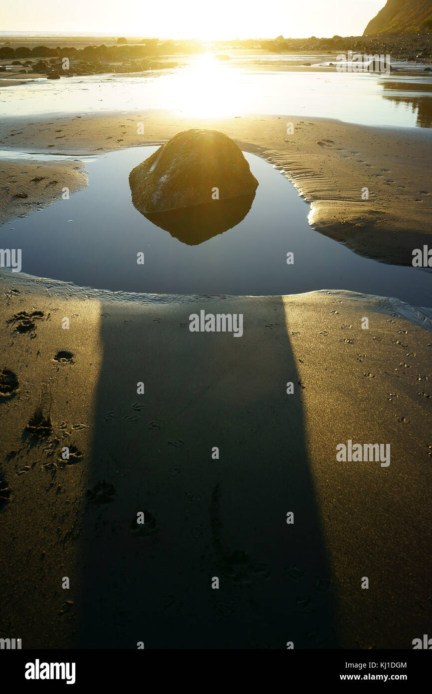 Boulder in tide pool throwing shadow at sunset at sand beach on low ...