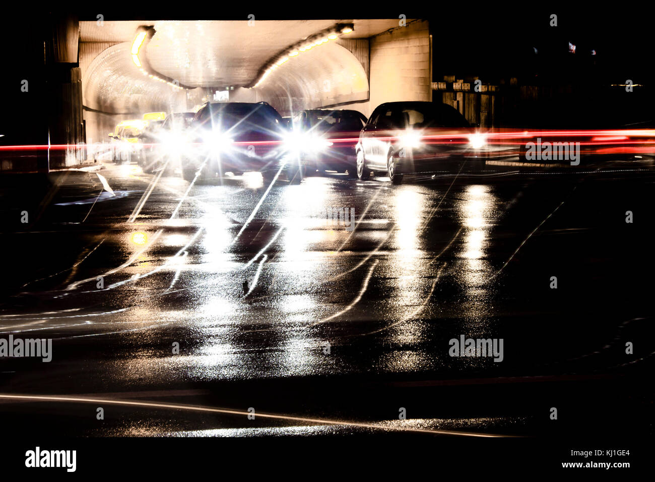Blurry night traffic on rainy city streets. Cars queued at tunnel exit ...
