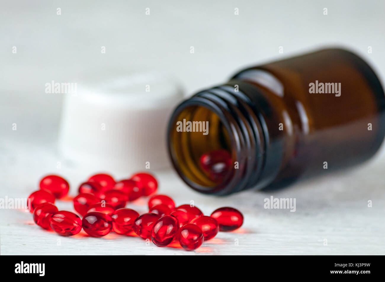 Red capsules with medicine or vitamins in liquid form lie on a white ...