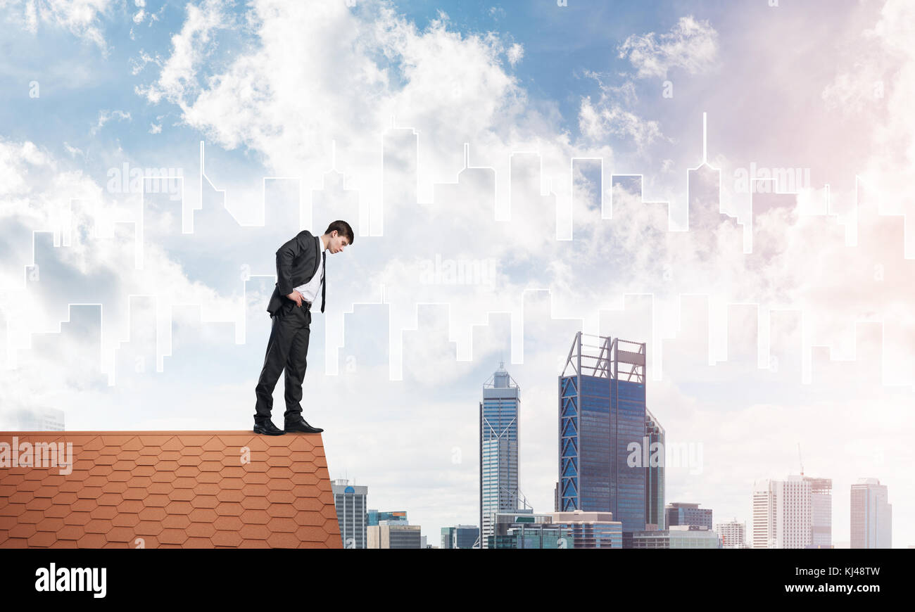 Businessman looking down from roof and modern cityscape at background ...