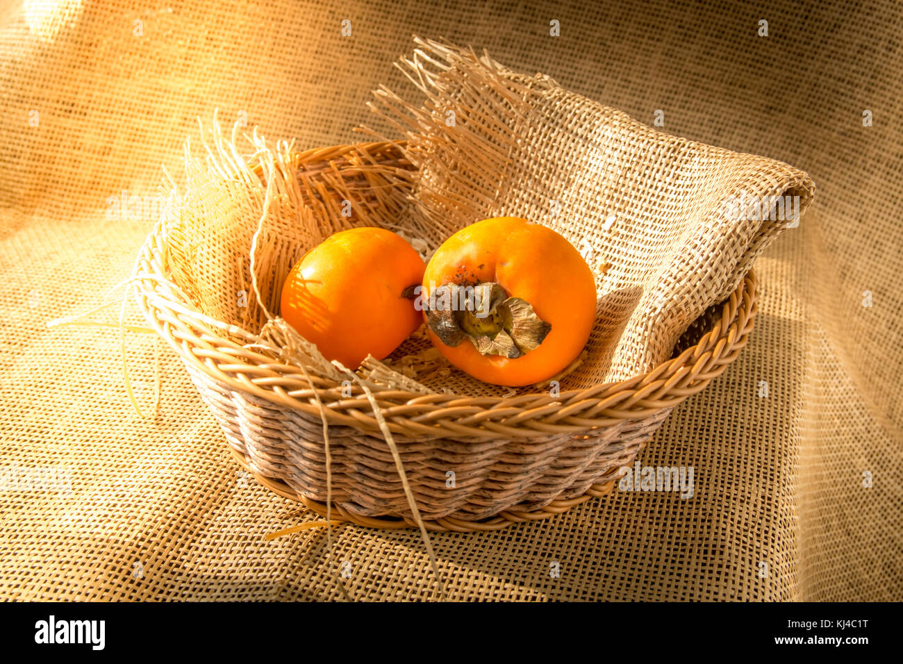 Delicious ripe persimmon fruit in basket wrapped with burlap textile ...