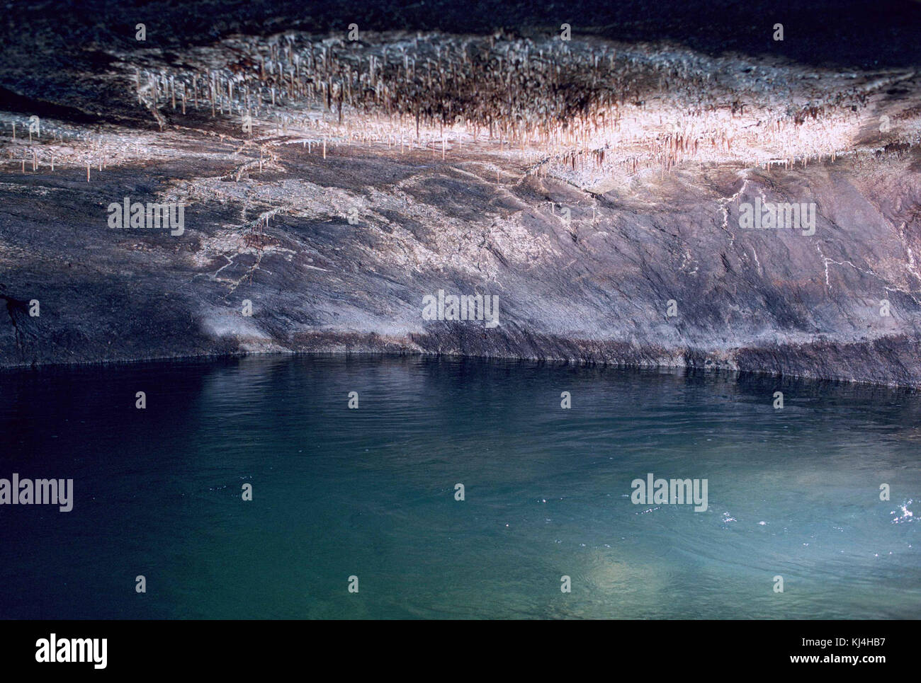 Cave interior flowing water with low ceiling and many small stalactites ...
