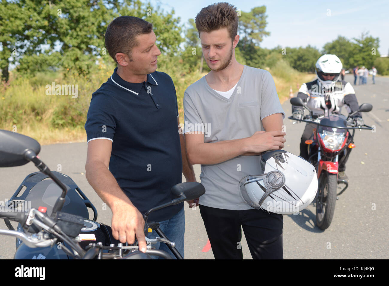 Man explaining motorcycle controls to young man Stock Photo - Alamy
