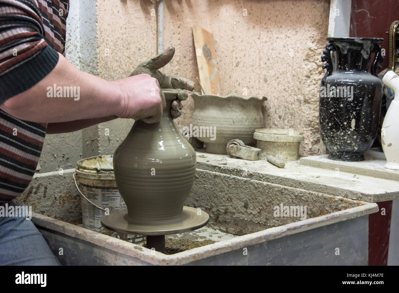 Man potter at work creating some traditional cups of white clay ...