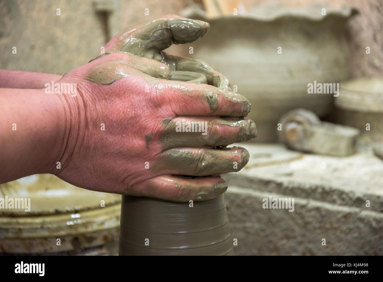 Man potter at work creating some traditional cups of white clay ...