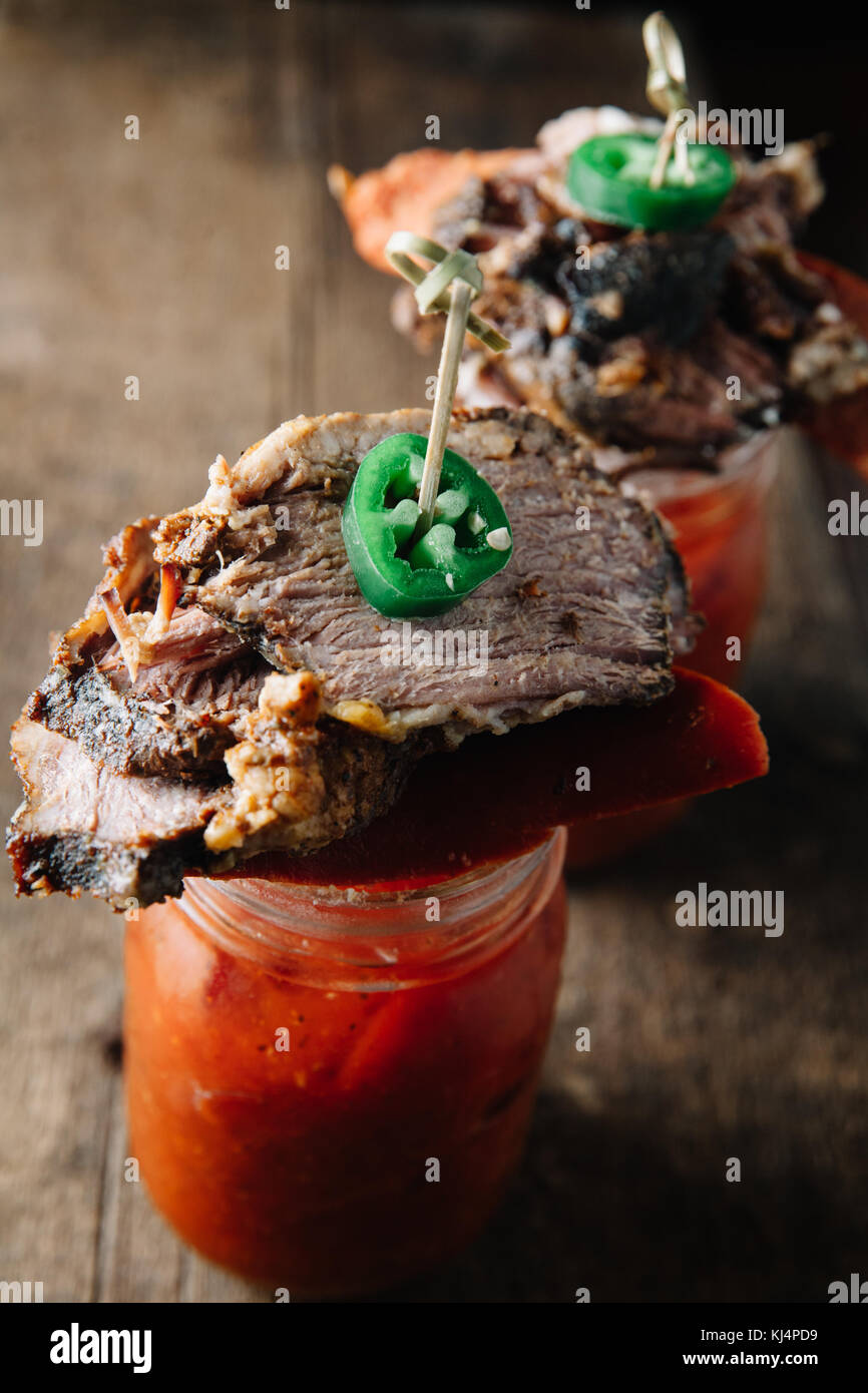 Two jars filled with bloody mary cocktail garnished with bbq meat on ...