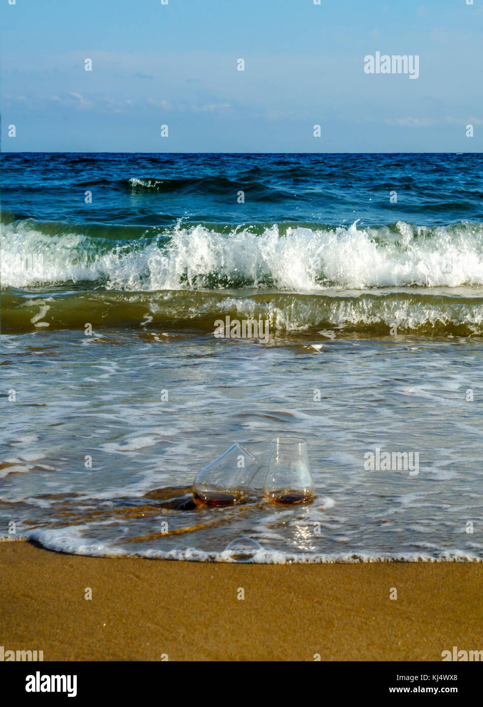 a glass of whiskey single malt on the sand washed by the waves, a glass ...