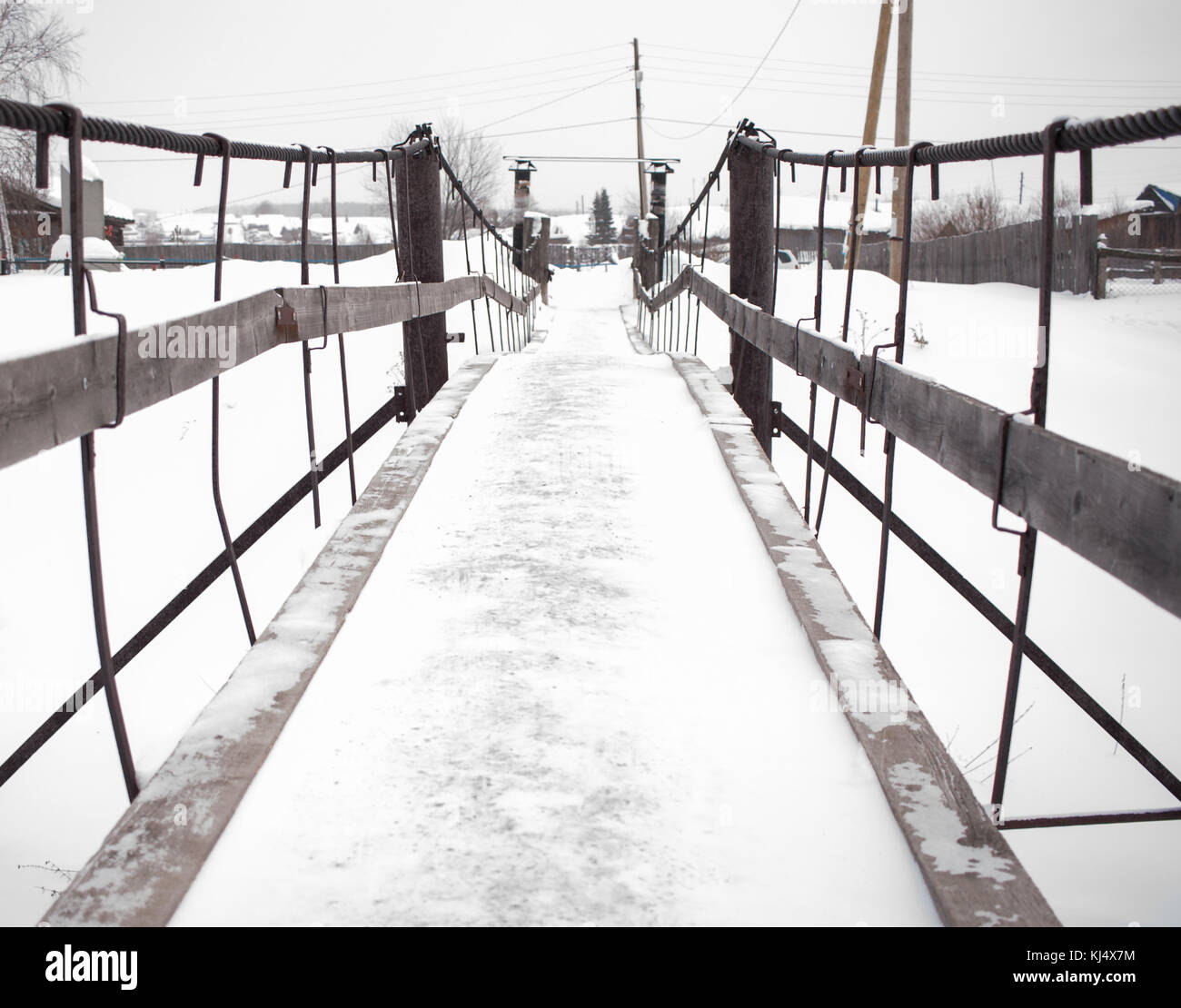 The narrow snow-covered bridge of metal and wood over frozen winter ...